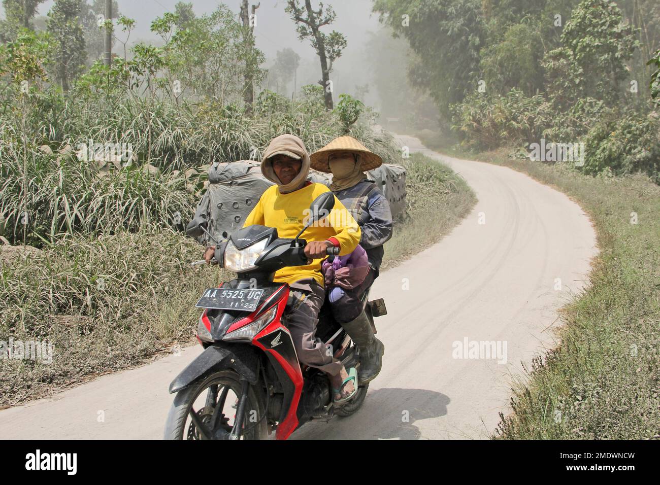 Local farmers ride a motorbike on a road covered in volcanic ash from ...