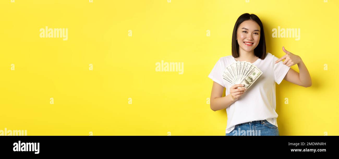 Young asian woman smiling, showing prize money, pointing finger at ...