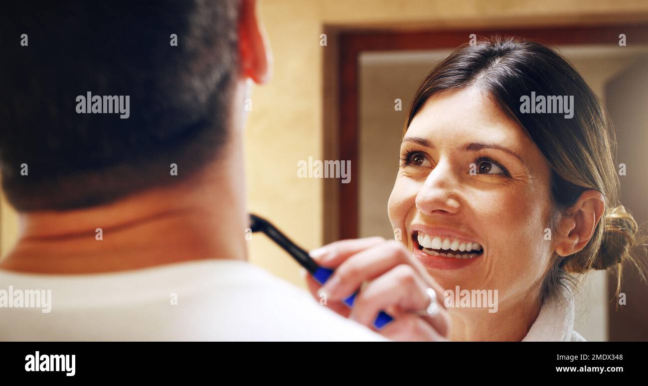 Helping her man get a clean shave. a woman shaving her husbands facial hair in the bathroom at ...
