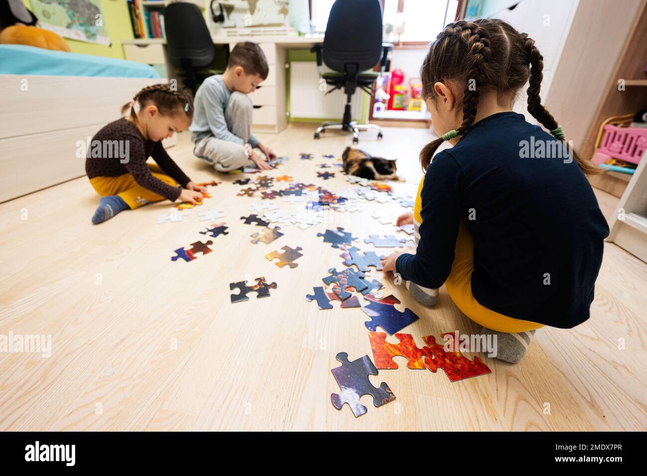 Children connecting jigsaw puzzle pieces in a kids room on floor at ...