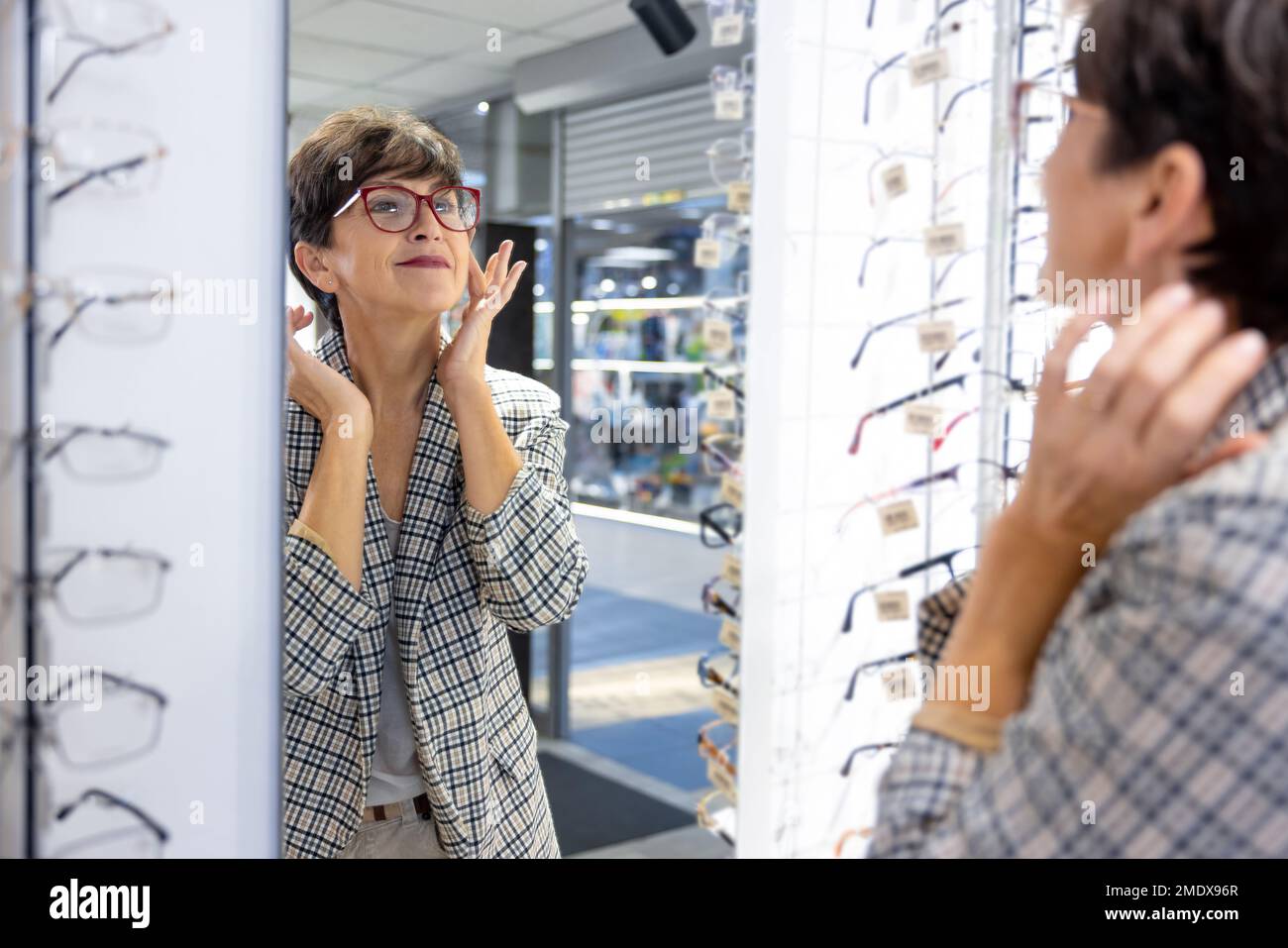 Mid aged good-looking lady trying on eyeglasses at the optical store ...