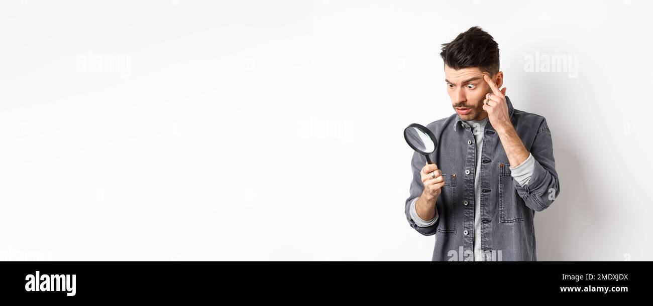 Man looking through magnifying glass and stretching eyelid to see ...