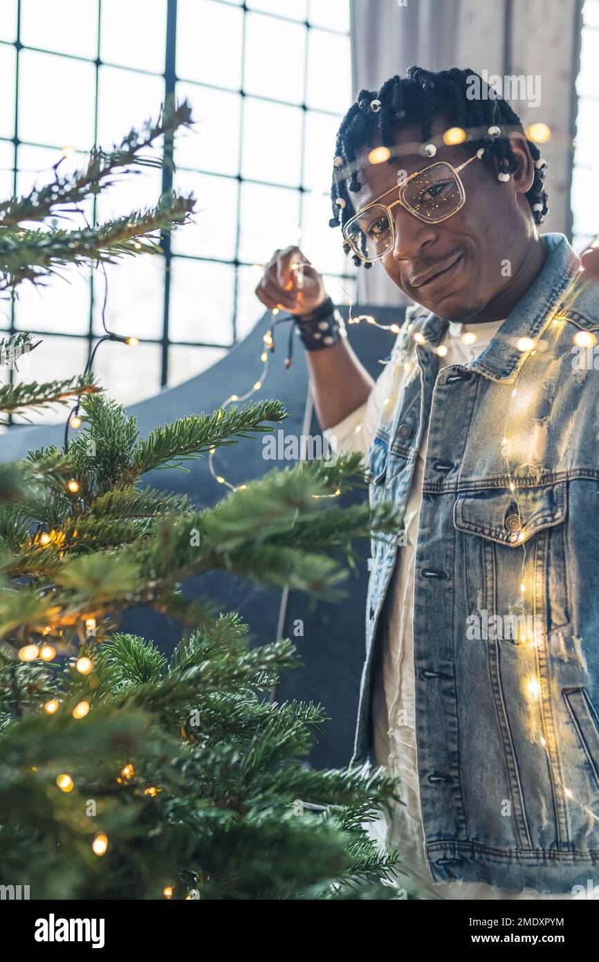 African American man decorating Christmas tree with fairy lights. High ...