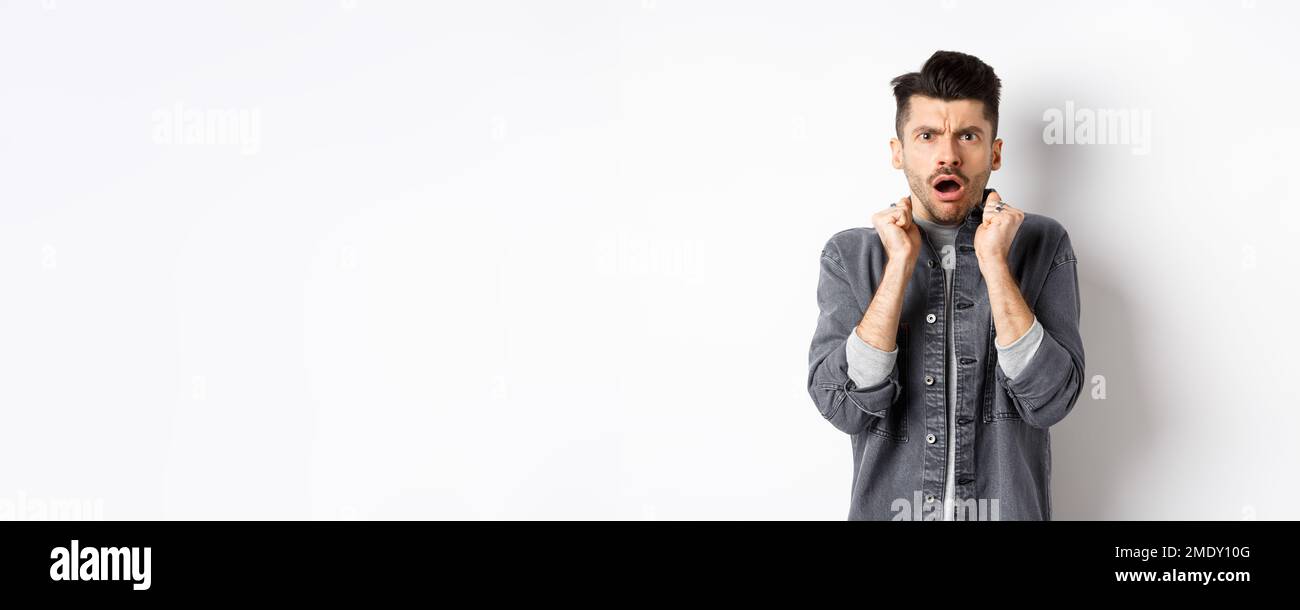 Shocked young man look confused and offended, gasping and frowning at ...