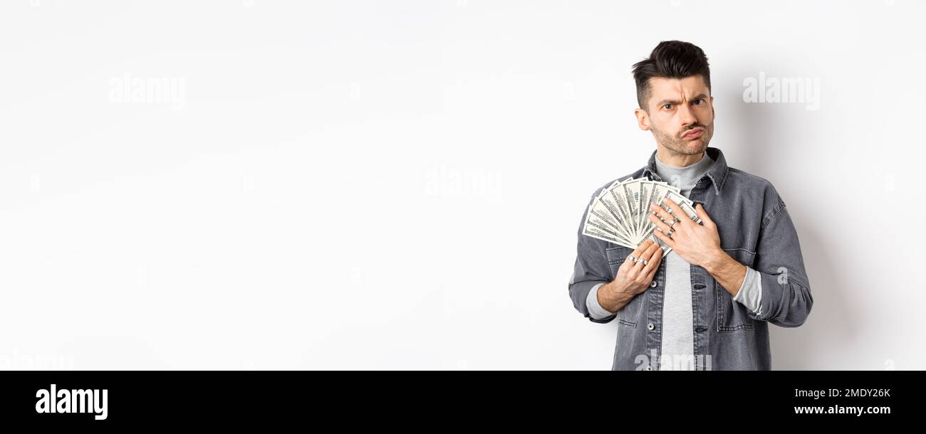 Greedy guy frowning and hugging dollar bills, unwilling to share money ...