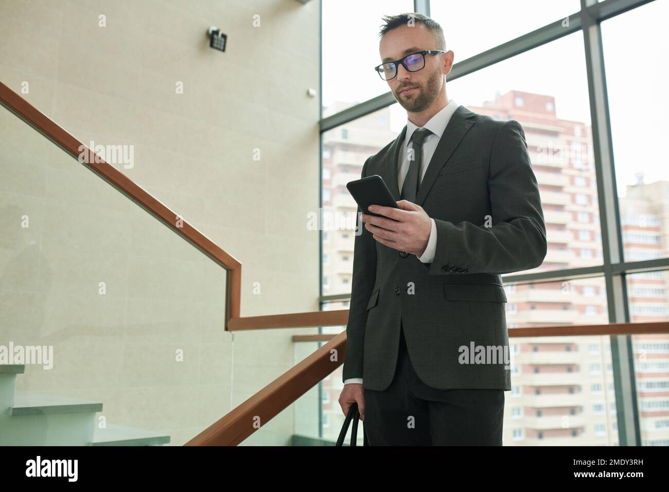 Young chief executive office in elegant suit and eyeglasses using ...