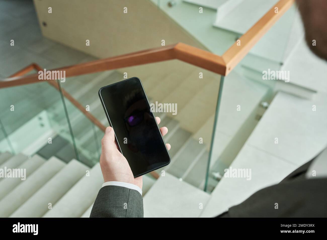 Hand of young businessman holding smartphone while standing on ...