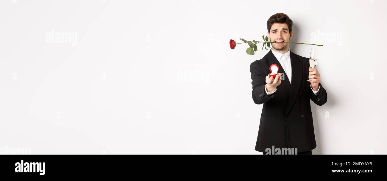 Romantic young man in suit making a proposal, holding rose in teeth and ...