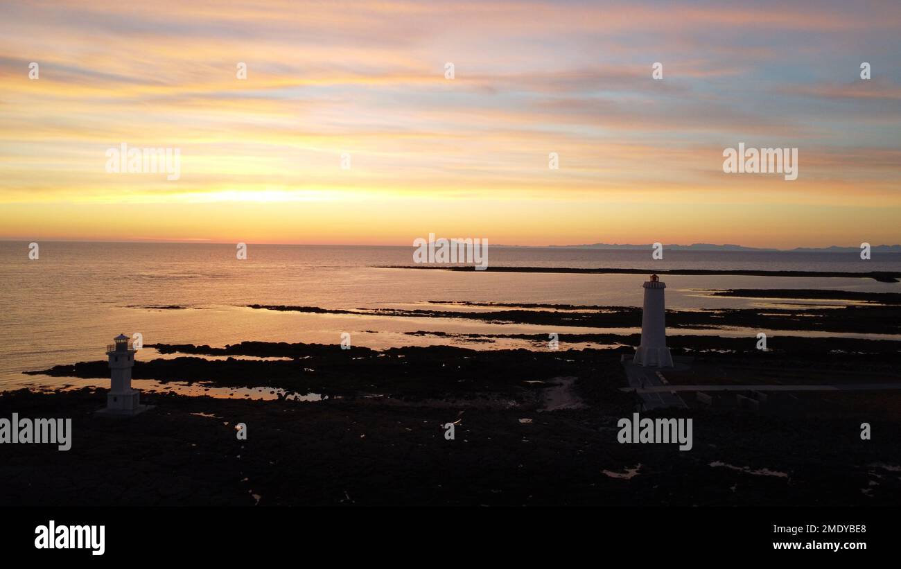 An aerial view of a lighthouse on the shore against colorful sunset sky ...