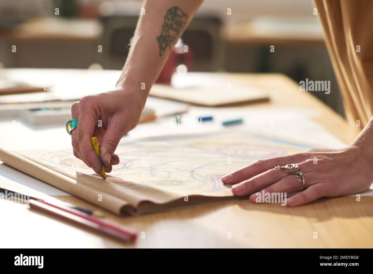 Hands of young craftswoman with yellow crayon drawing on page of big ...