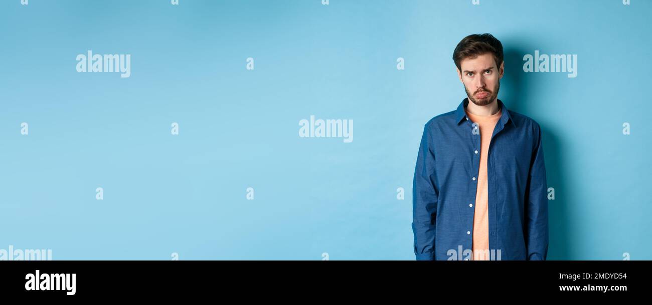 Sad and gloomy young man sulking, pulling miserable face and looking ...