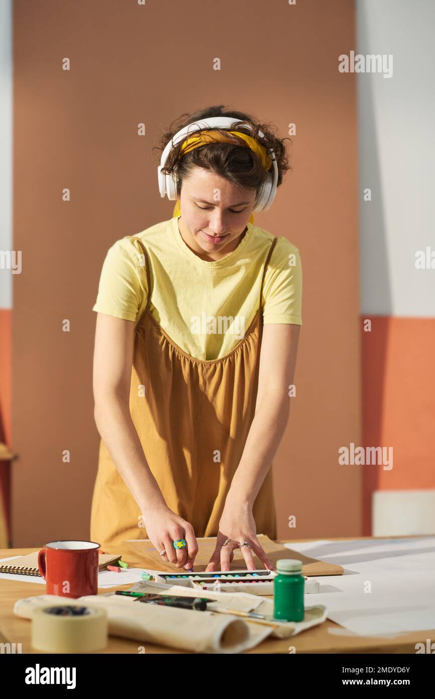Young serious craftswoman with headphones enjoying her favorite music ...