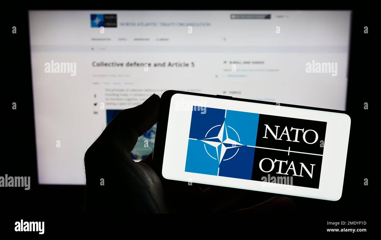 Person holding mobile phone with logo of North Atlantic Treaty ...