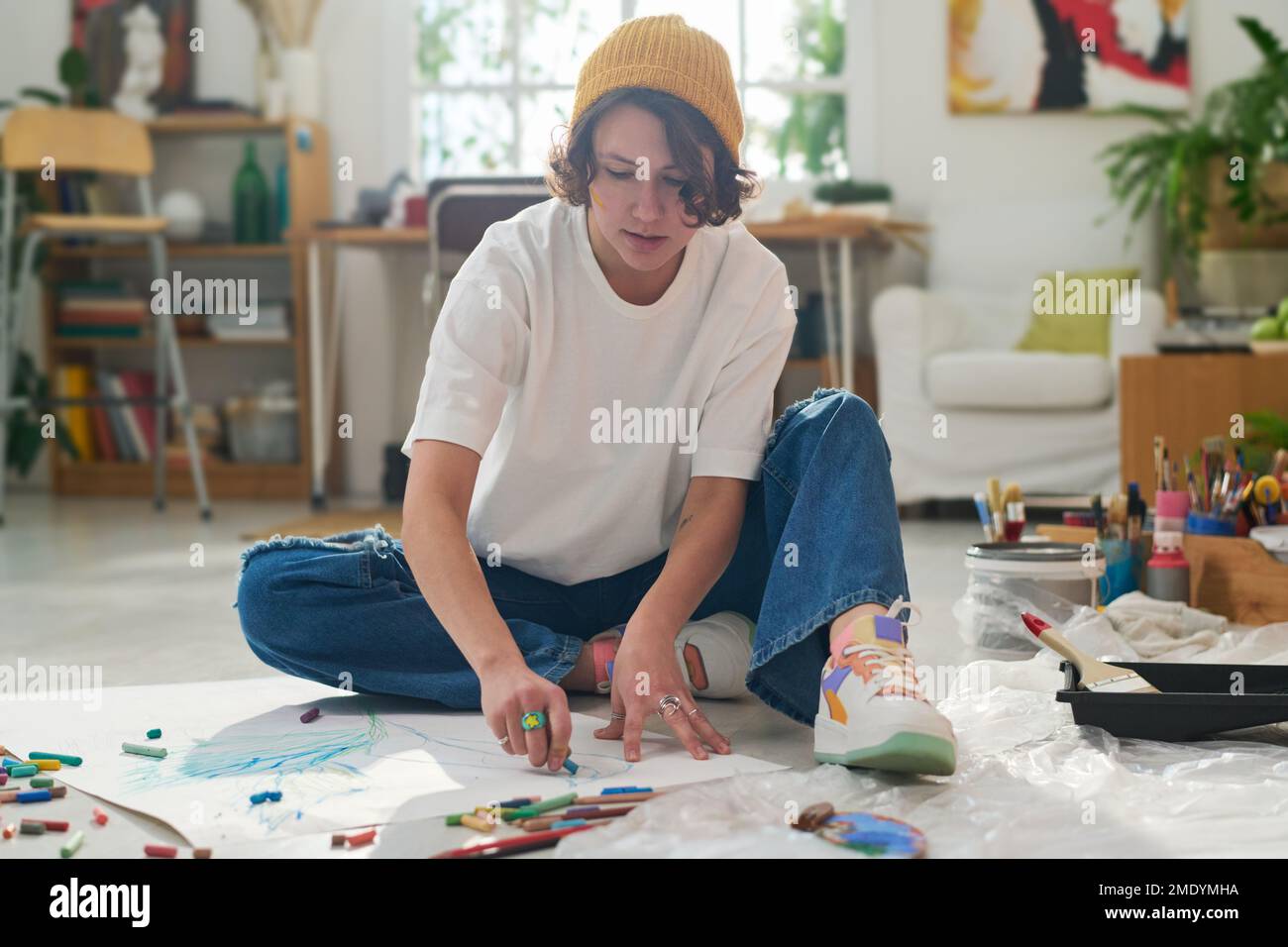 Young female artist or designer with blue crayon drawing on paper while ...