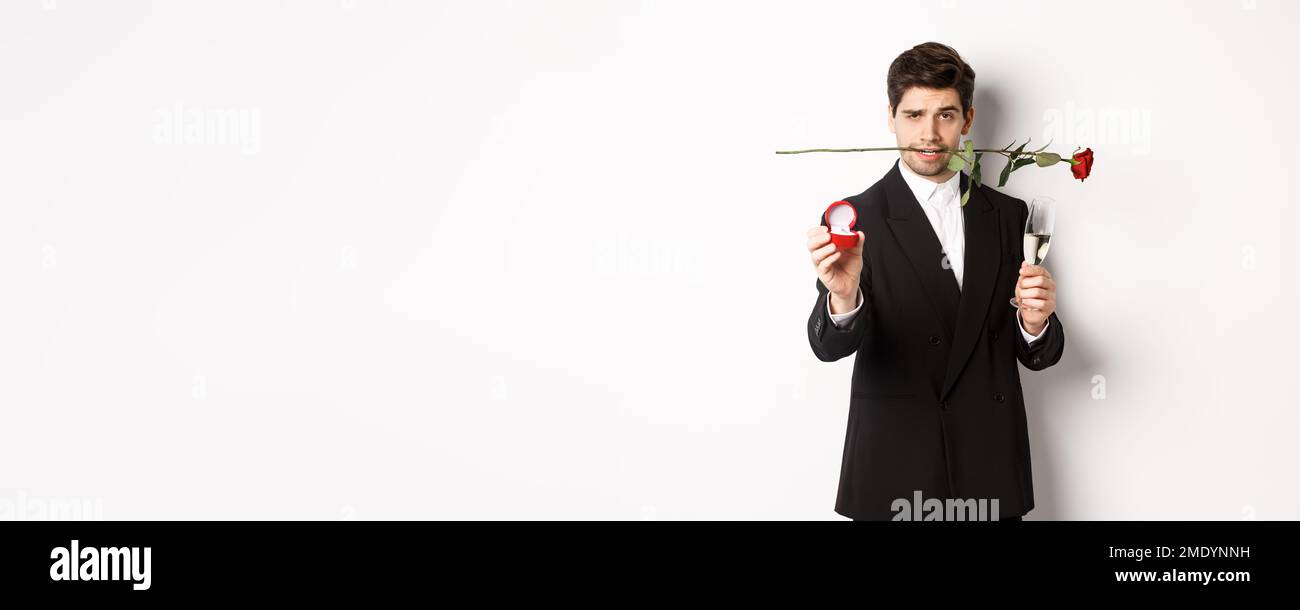 Passionate young man in suit making a proposal, holding rose in teeth ...
