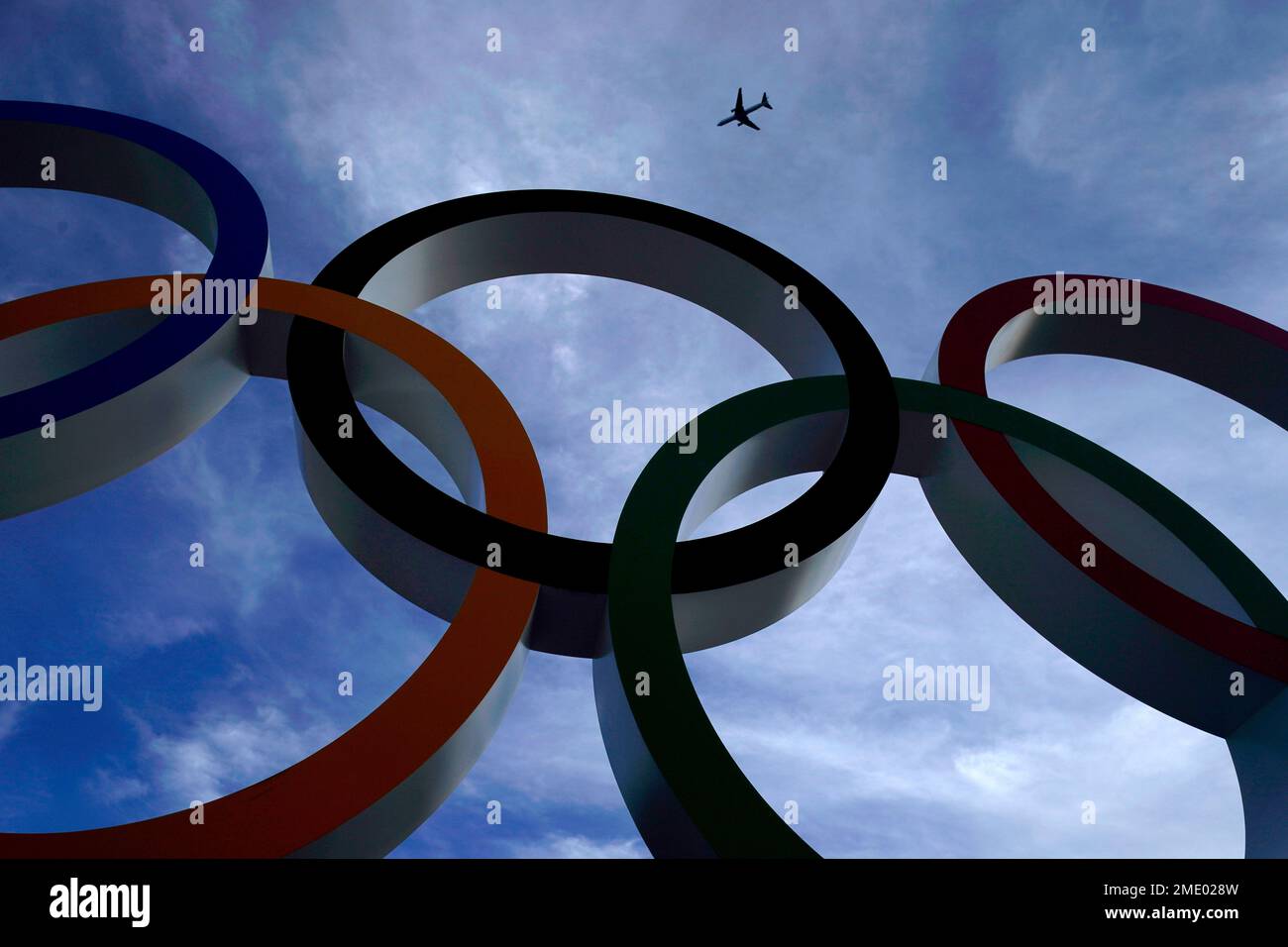 A passenger jet flies over the Olympic rings on display outside the ...