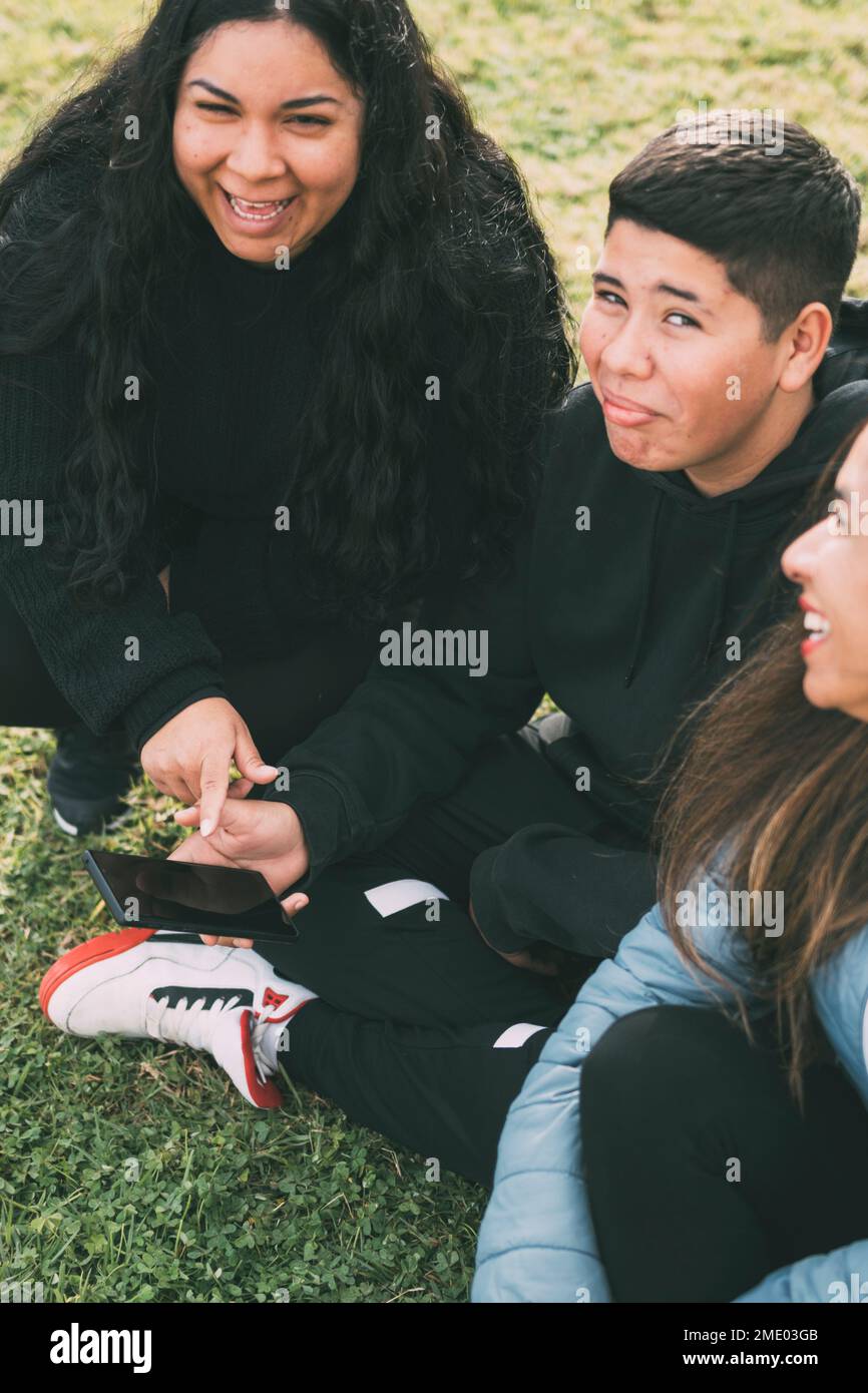 group of Latinos laughing sitting on the ground in a park with a ...