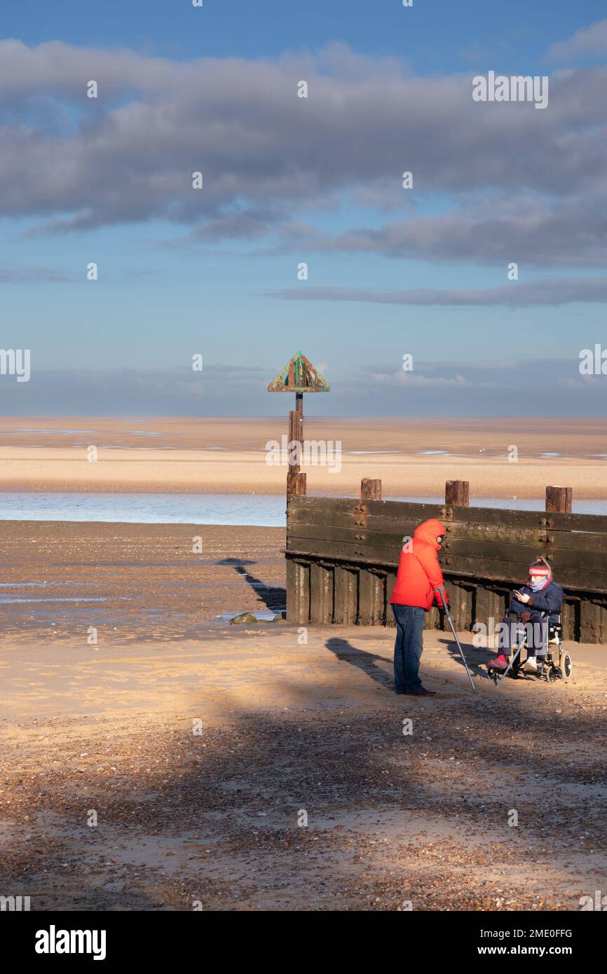 Lady in wheelchair and person with crutch walking aid on beach during ...
