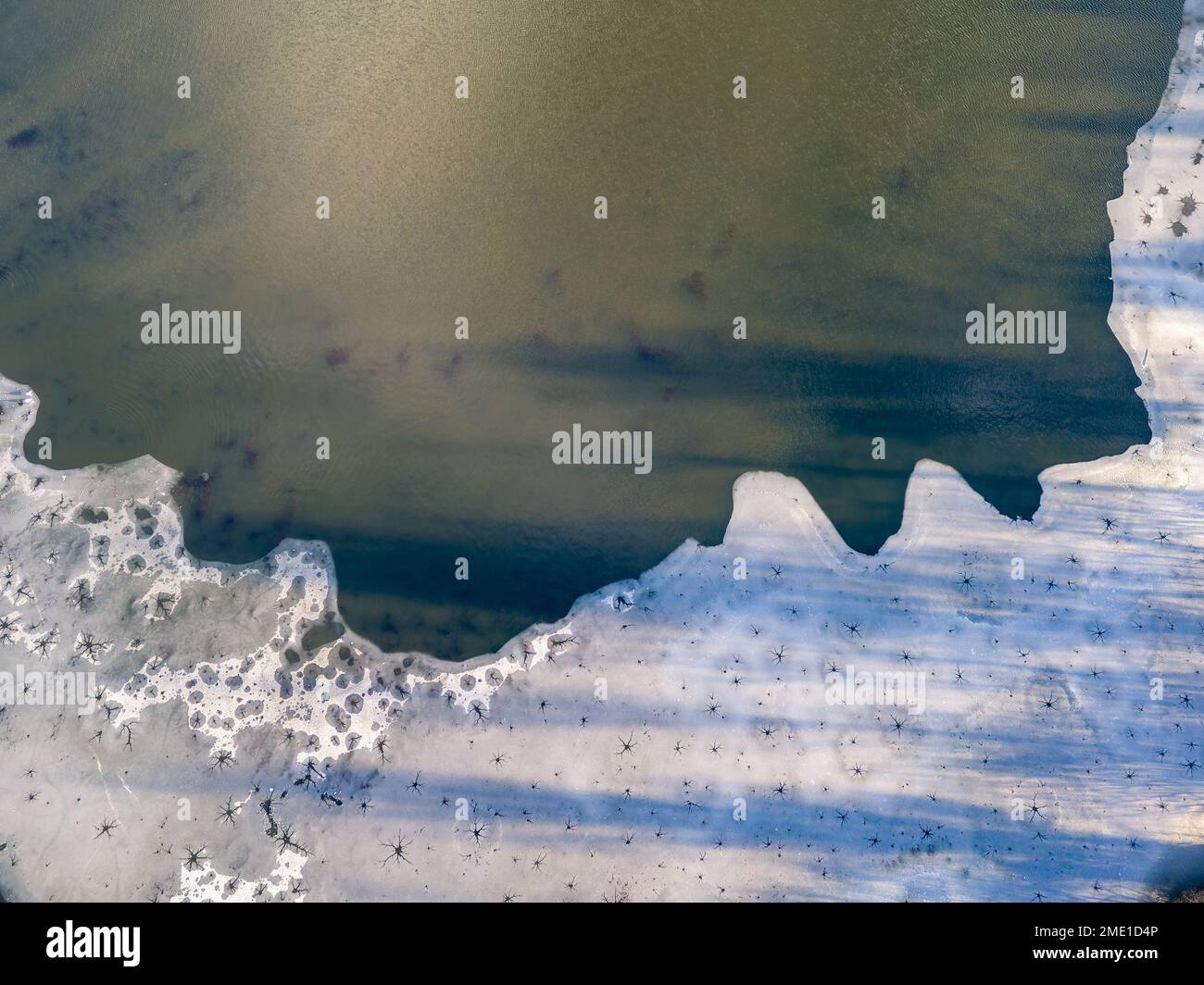 Top down aerial view of ice forming on a freezing lake surrounded by ...