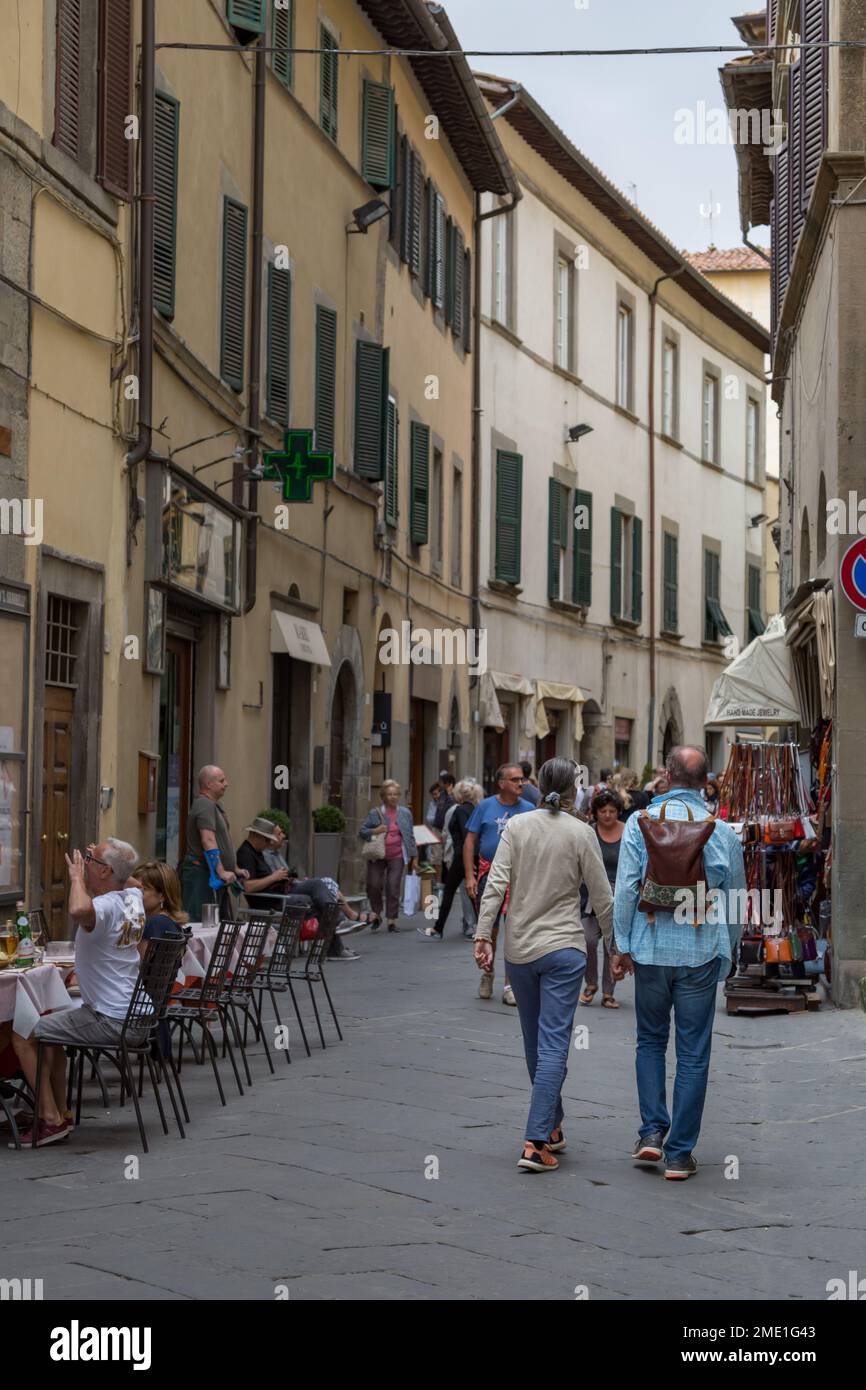 Middle-aged couple (man and woman) holding hands walking down via Nazionale in Cortona, Tuscany ...