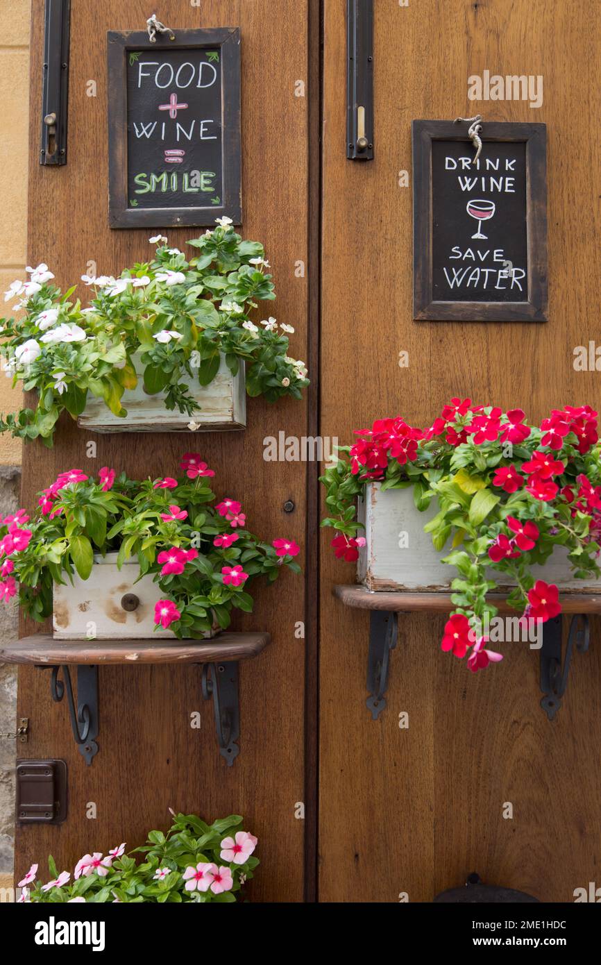 Potted flowers and wine signs hanging on wall outside of shop in ...