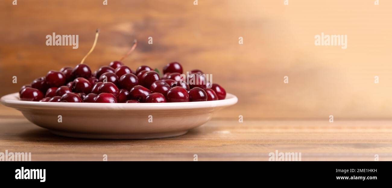 ripe red cherries in a white plate on a wooden background with copy ...