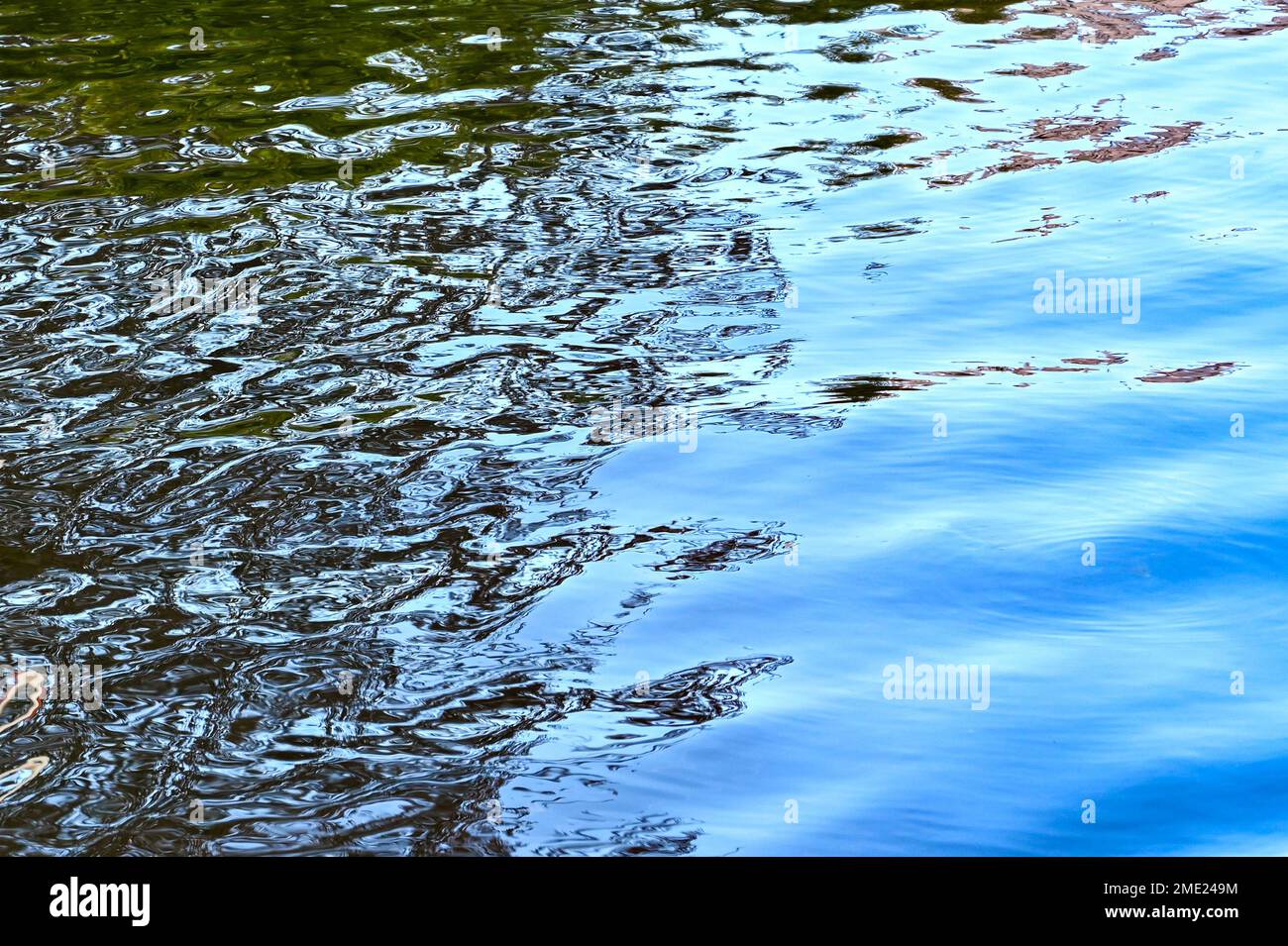 Pattern formed by the reflection of trees and a blue sky on rippled ...