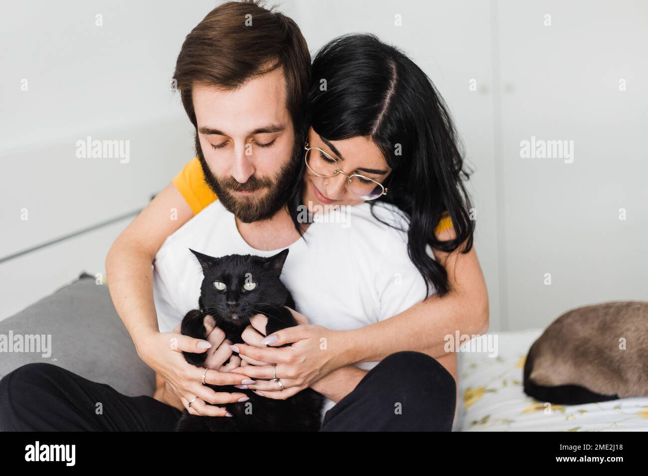 Calm young couple in domestic outfits hugging and caressing cute black ...