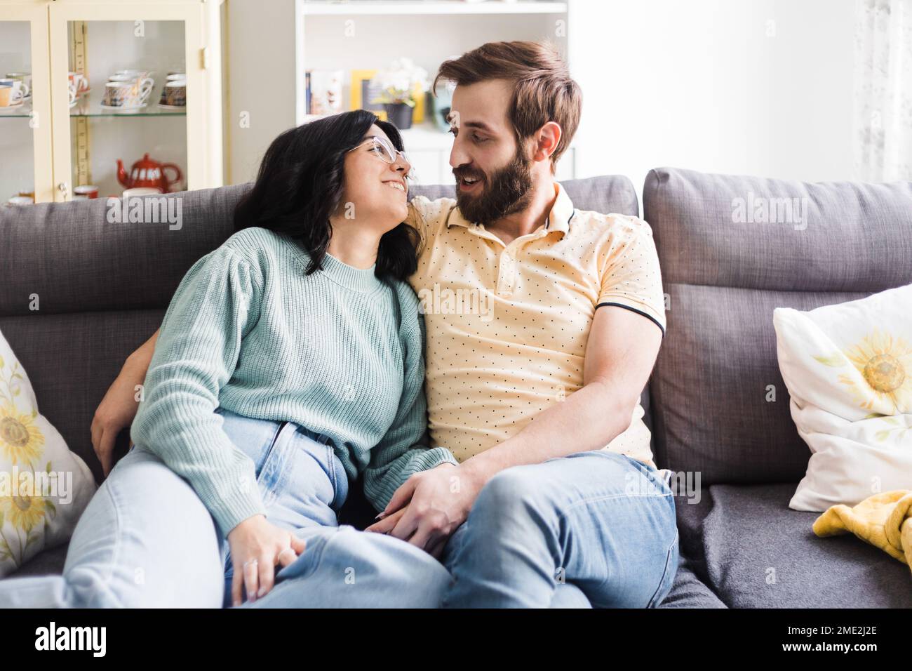 Cheerful young couple in casual outfits smiling and looking at each ...