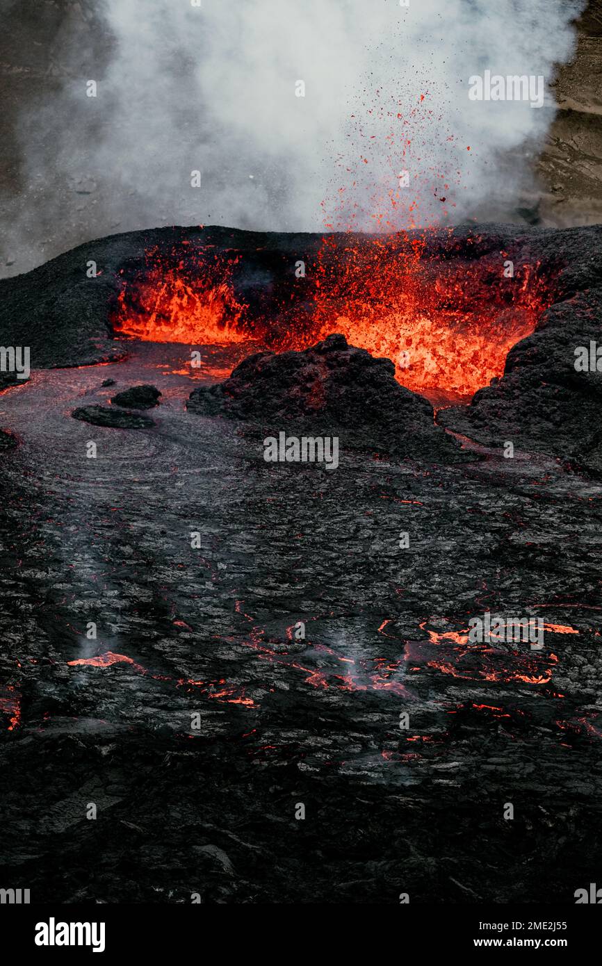 Splashes of hot orange lava erupting from volcanic mountain peak ...