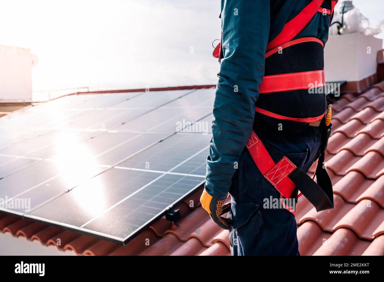 Side view of faceless man in working harness standing on tiled roof ...
