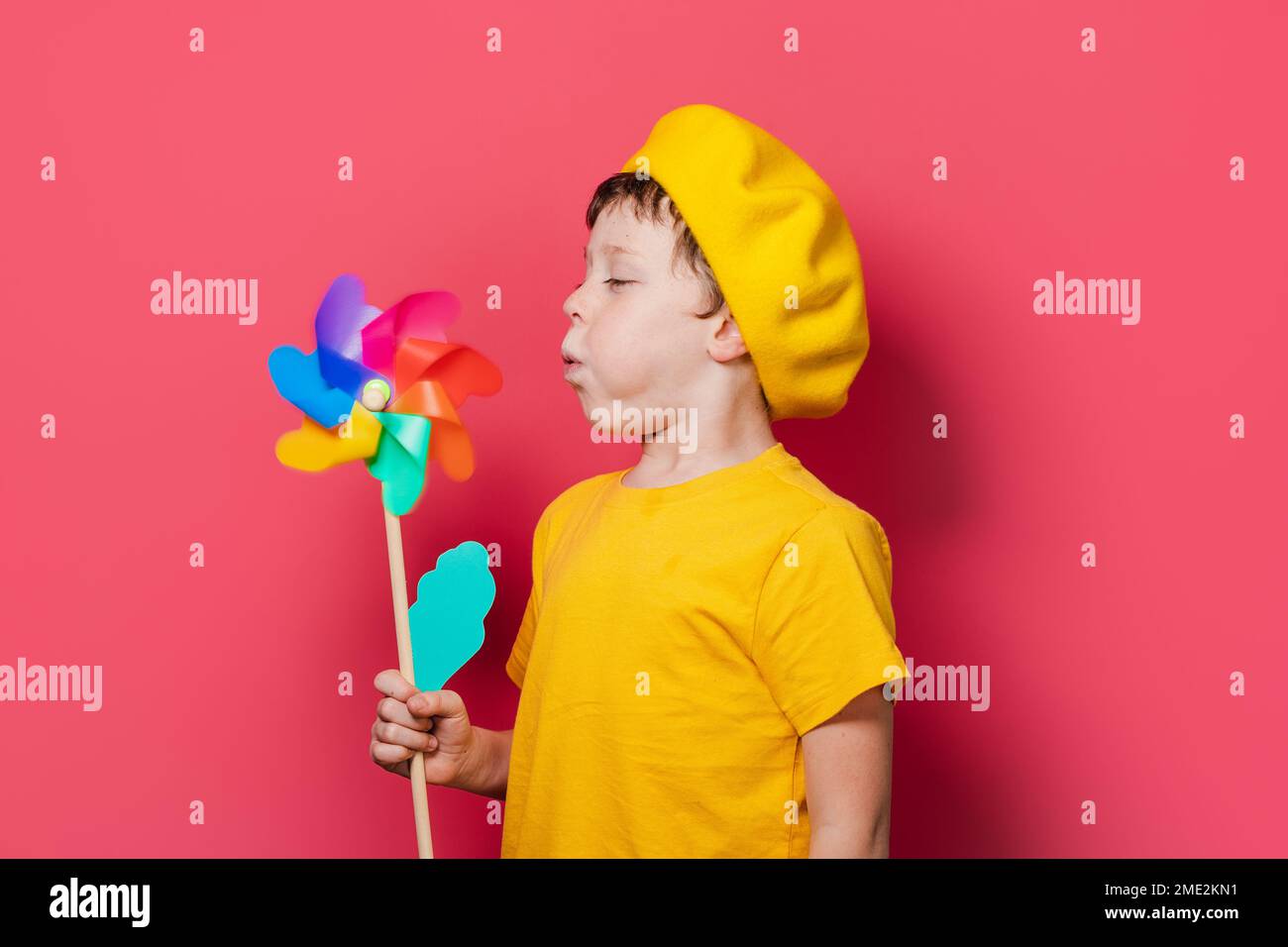 Boy in yellow t shirt and hat standing against pink background and ...