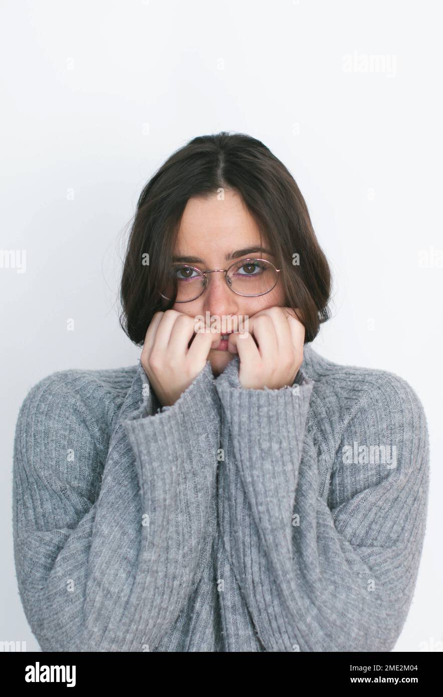 Worried female with dark hair in warm gray sweater and glasses standing ...