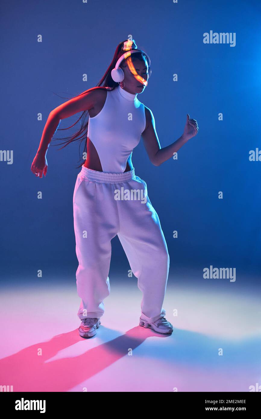 Full body of young female in white bodysuit and pants moving to music ...