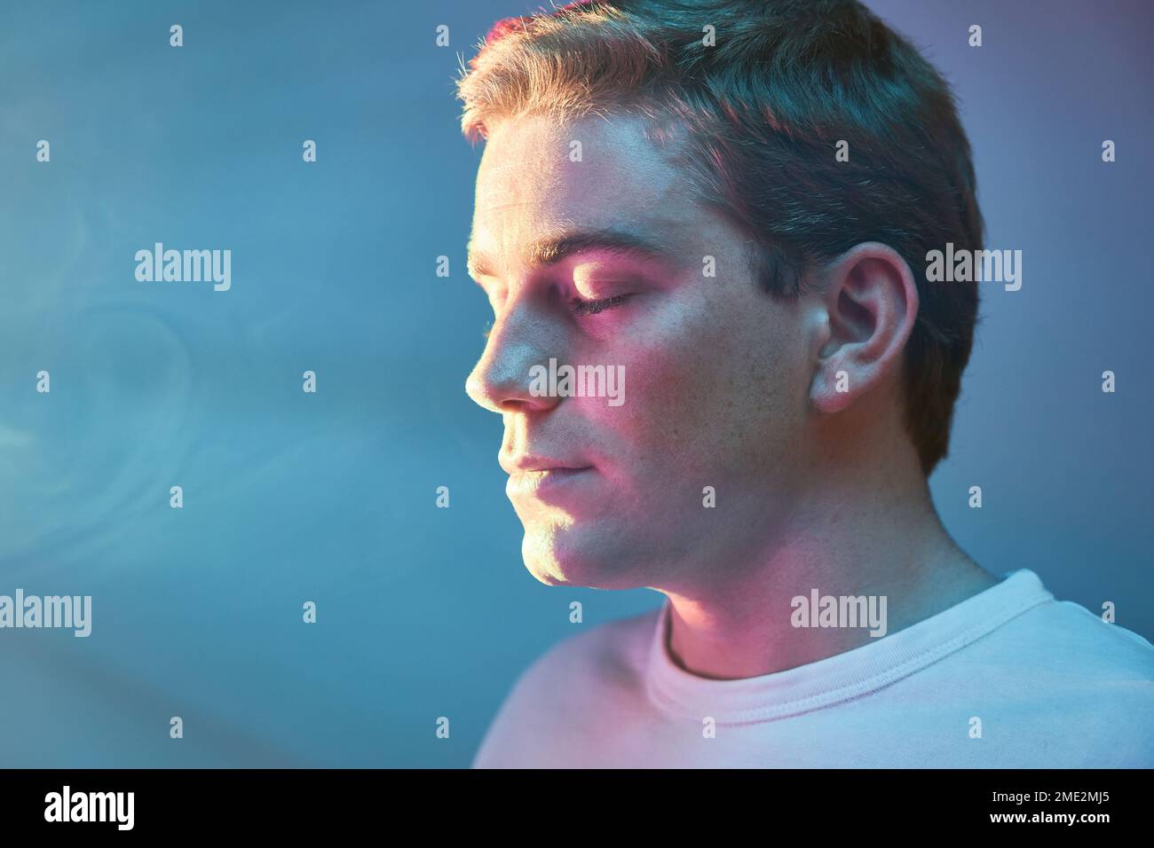 Handsome young male with closed eyes and short haircut standing in neon ...