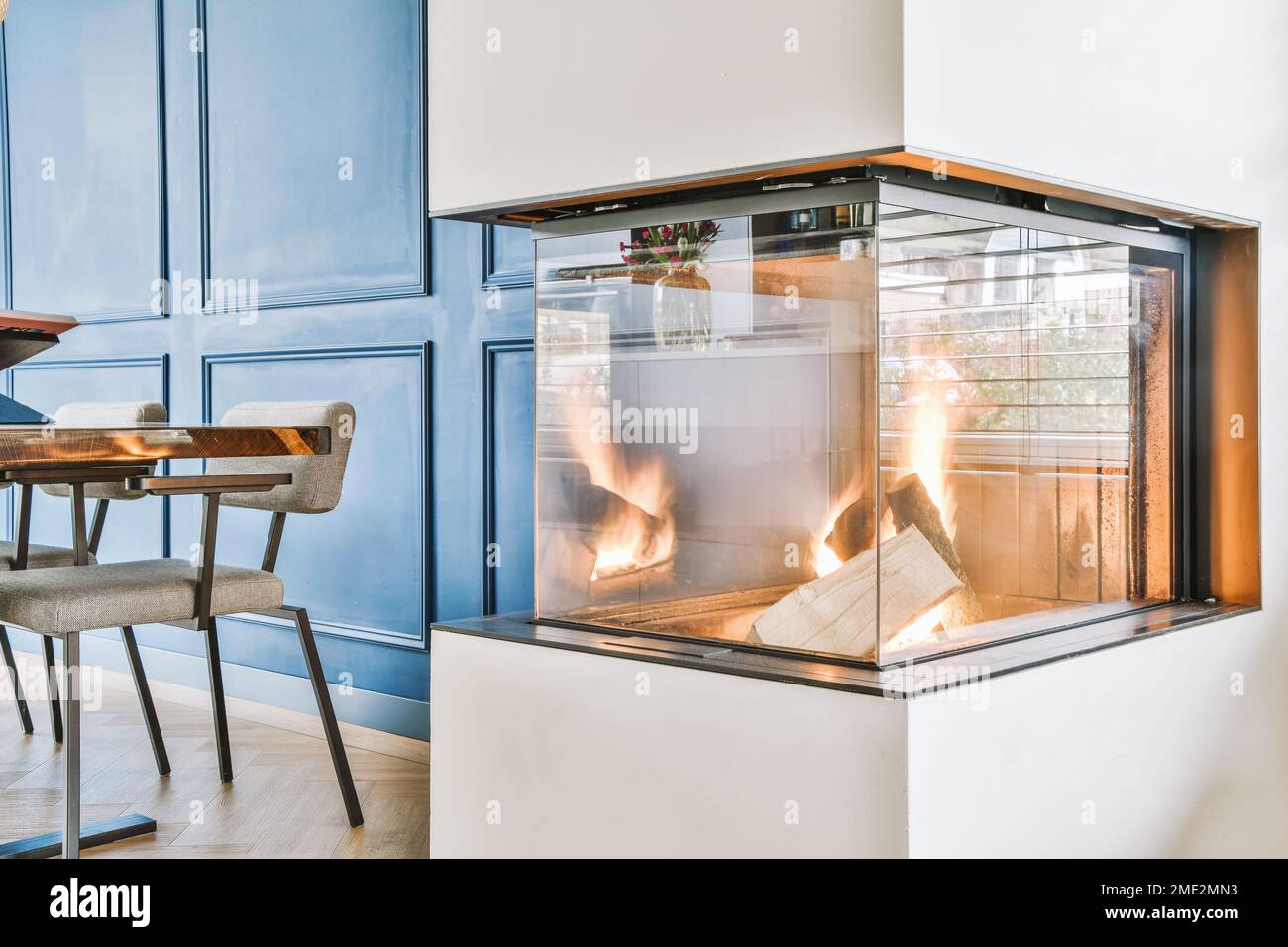 Cubical glass fireplace with burning logs located near dining table in ...