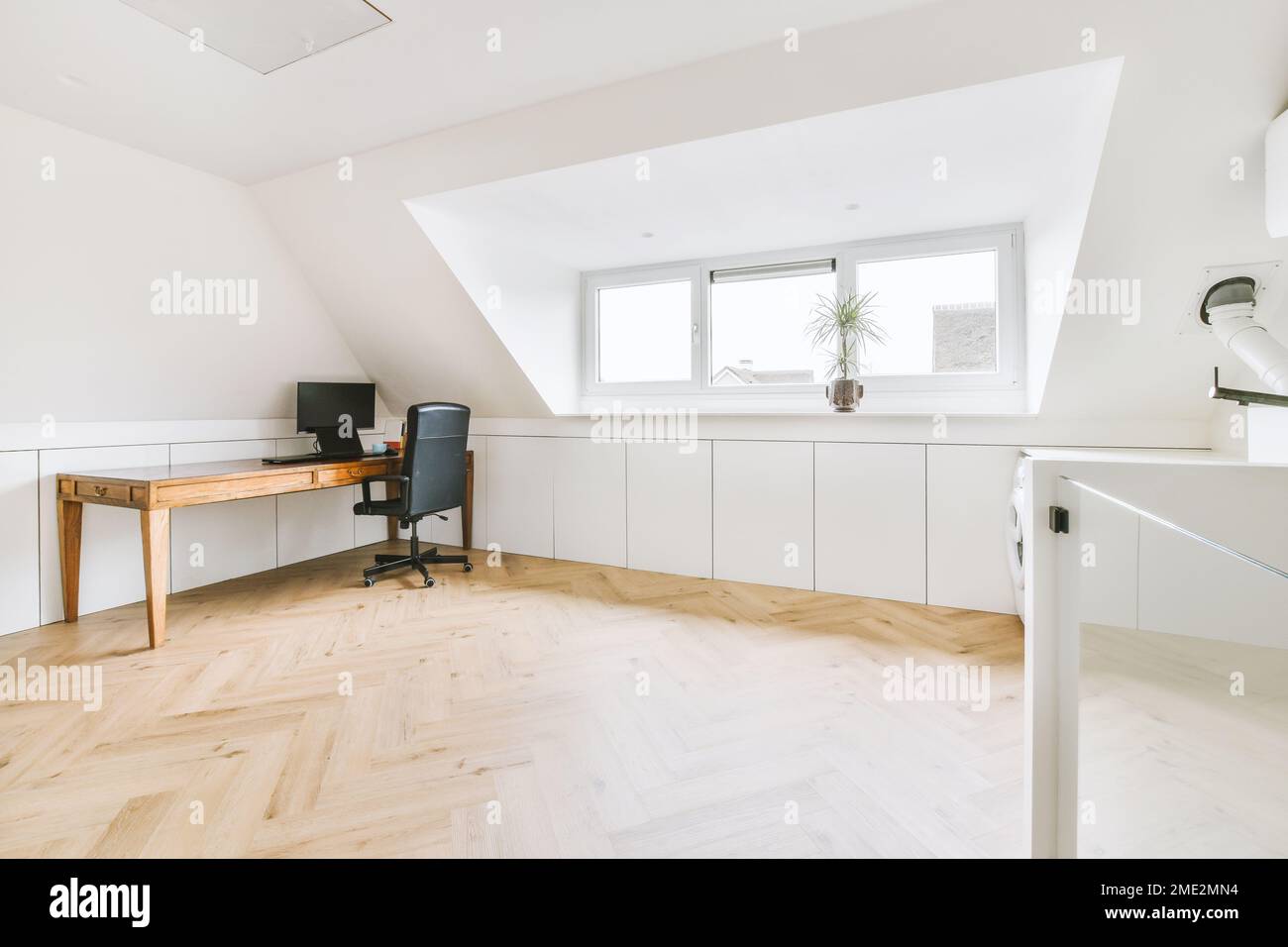 Desk with computer and chair located near window in sunlit attic home ...
