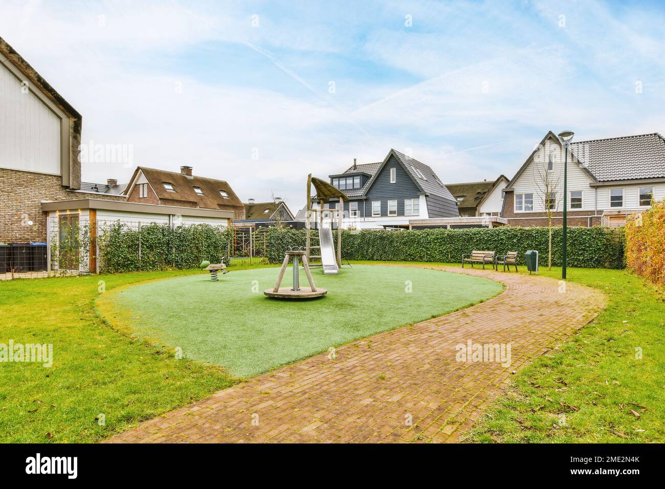 Curvy paved path and playground located on grassy lawn near hedge and ...