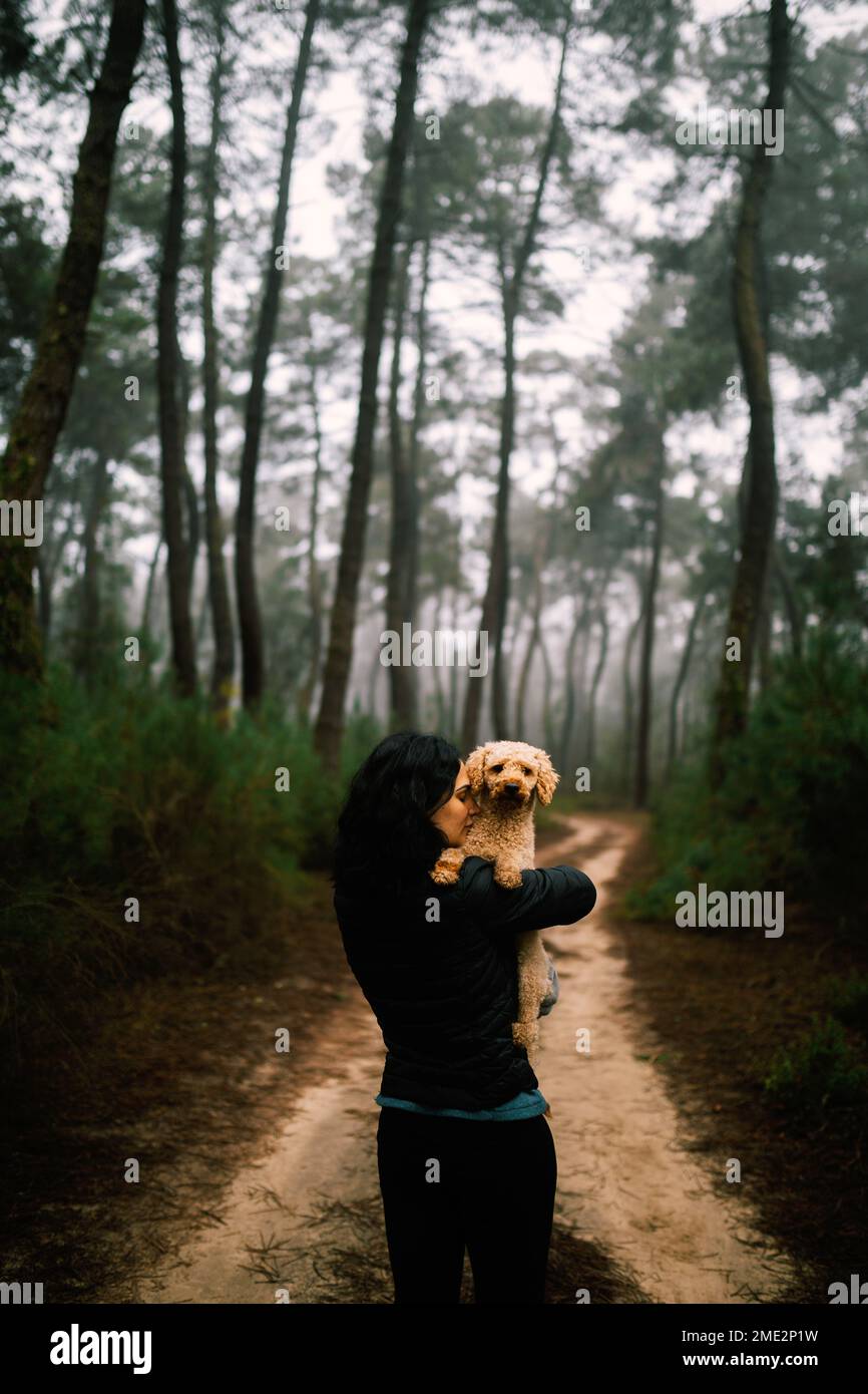 Back view of female owner with adorable puppy on shoulder standing with ...