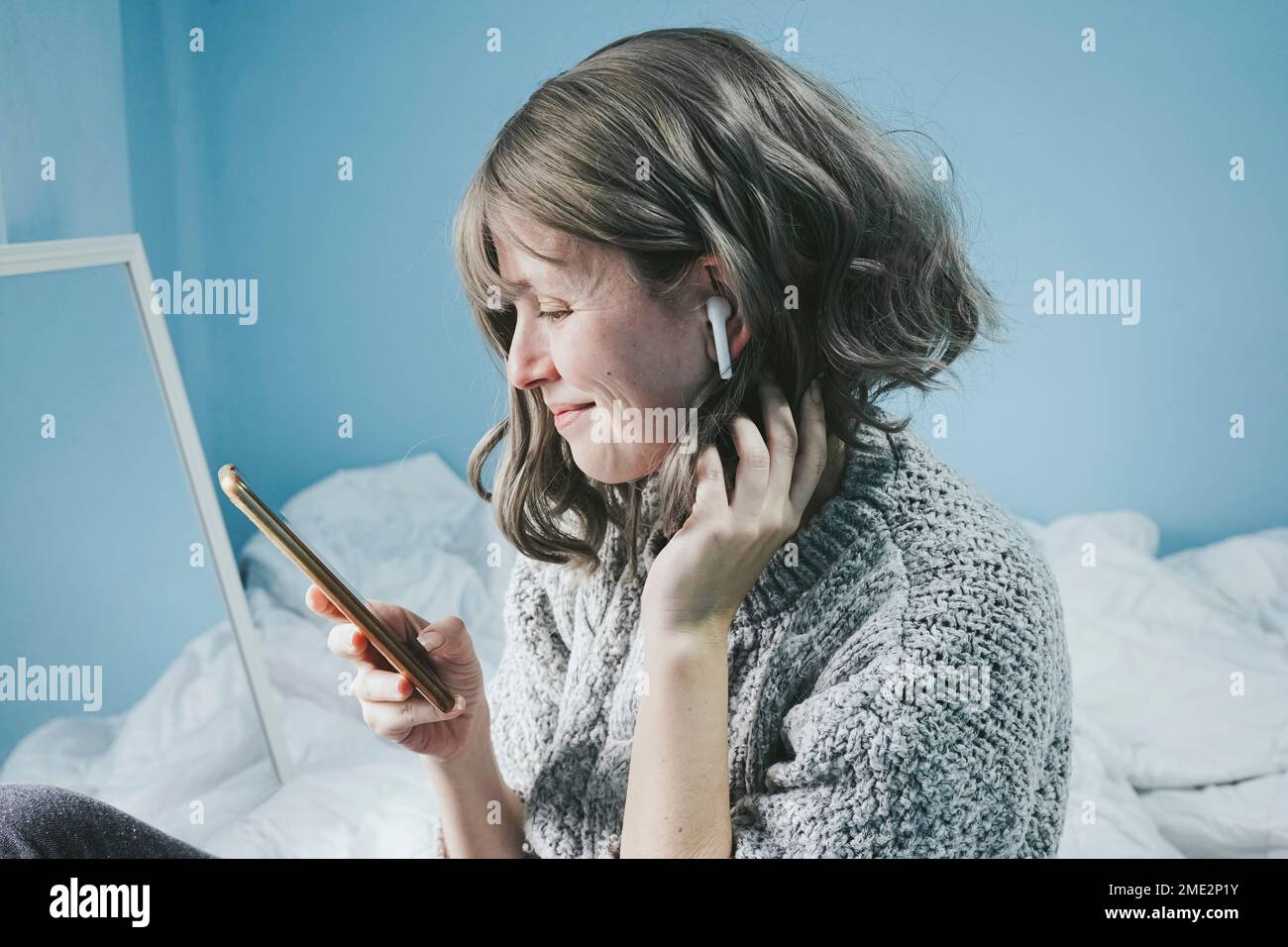 Positive side view of adult female with short gray curly hair in warm sweater sitting on ...
