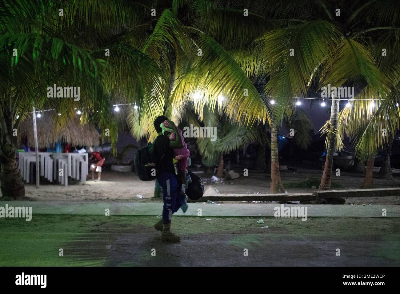 A migrant carries a baby through Necocli, Colombia, before dawn ...