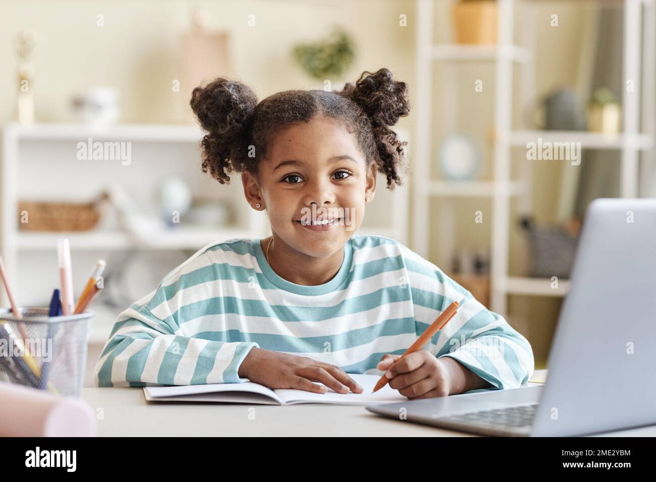 Portrait of cute black girl doing homework at desk and smiling at ...