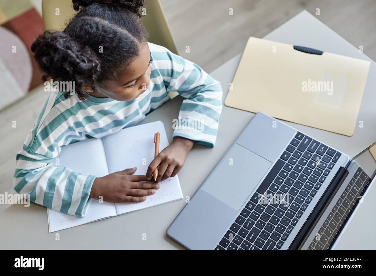 Top view portrait of cute black girl doing homework at desk and looking ...