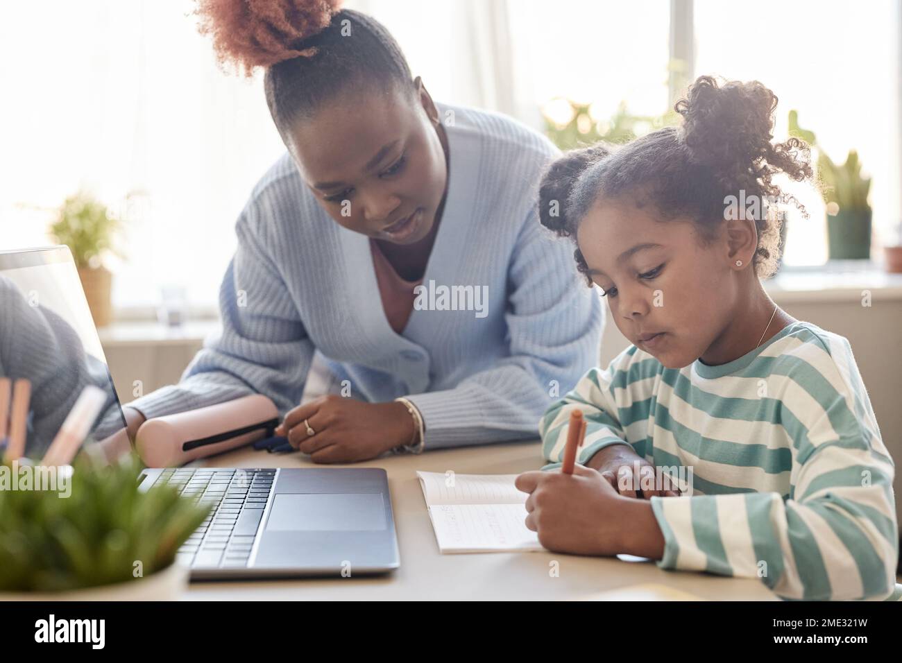 Portrait of black young teacher tutoring little girl studying at home ...