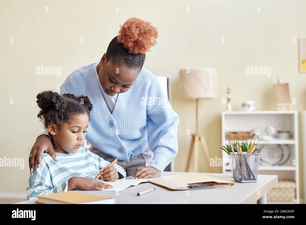 Minimal portrait of caring mother helping little black girl studying at ...