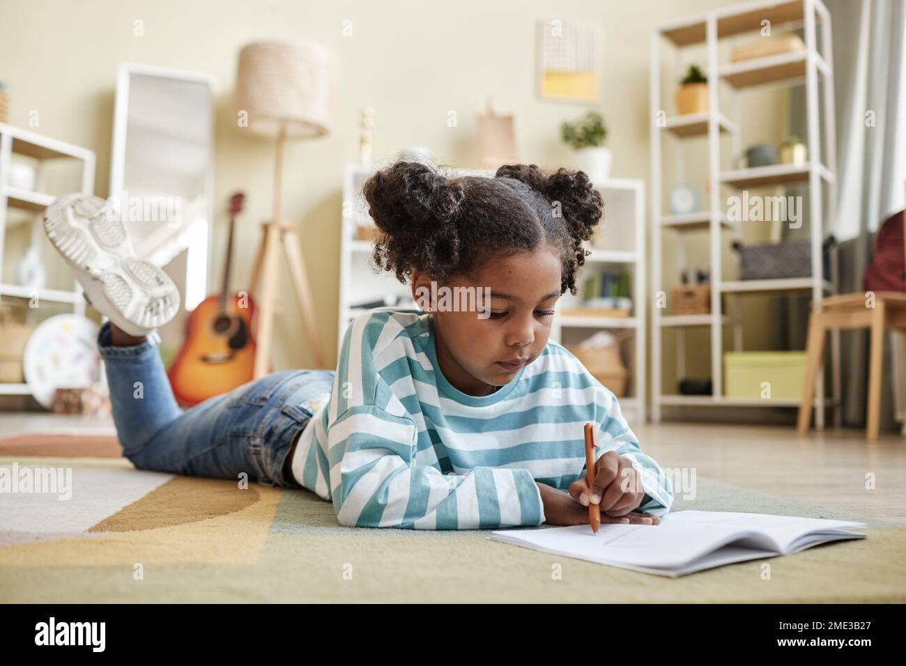 Full length portrait of cute black girl laying on floor at home and ...