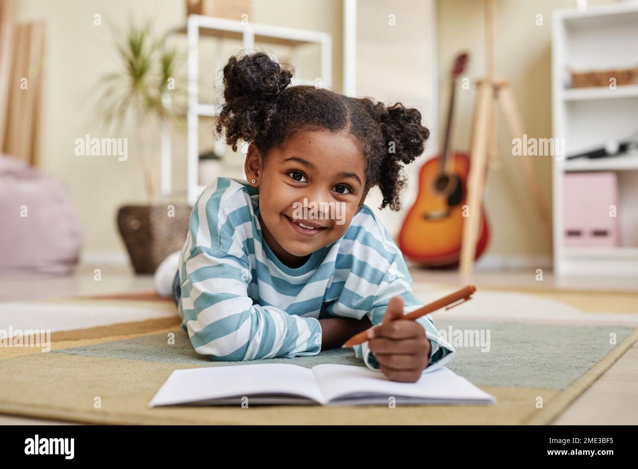 Front view portrait of cute black girl laying on floor at home and ...