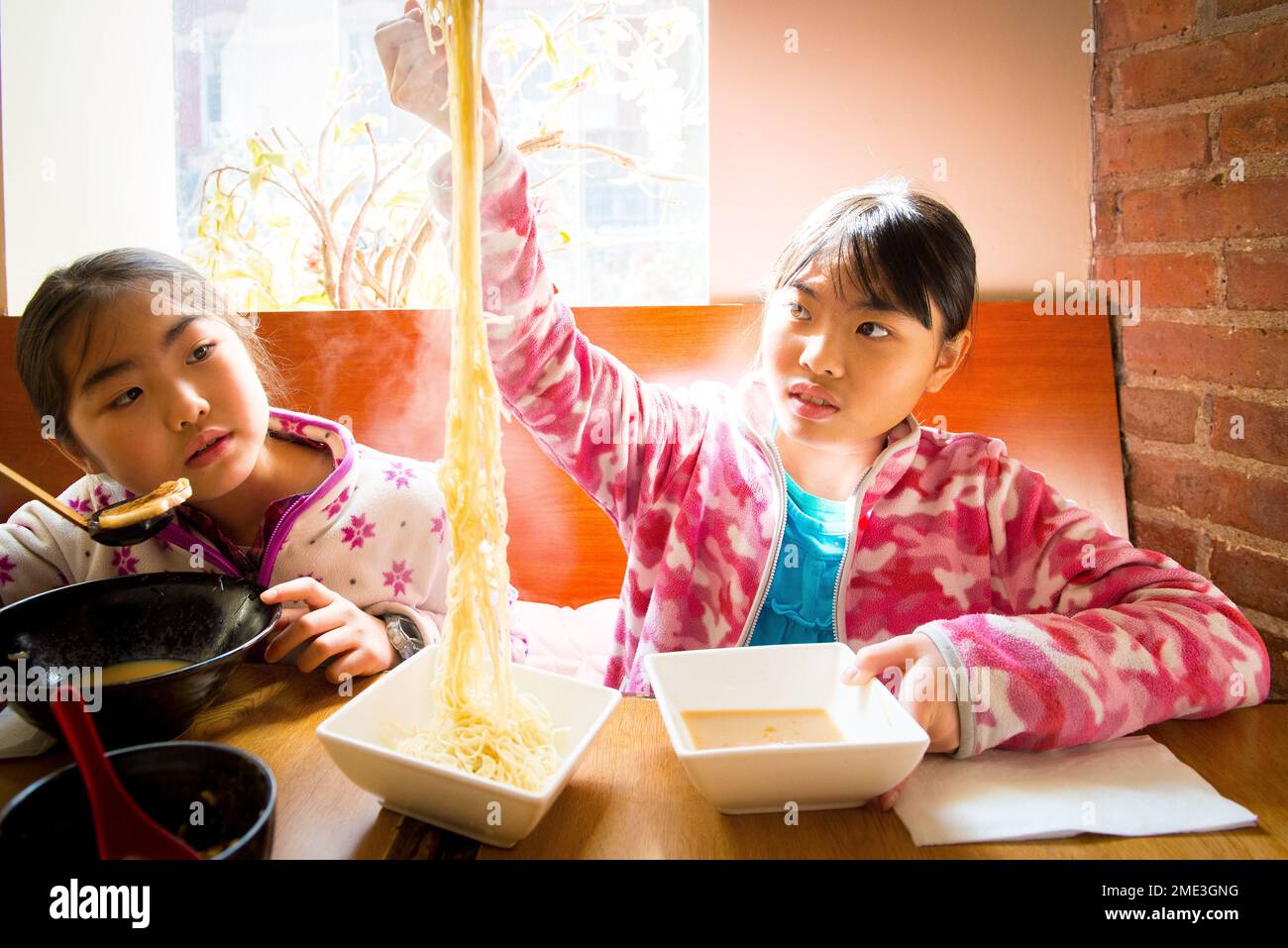Asian girl eating ramen at a local restaurant - stretching long noodle ...