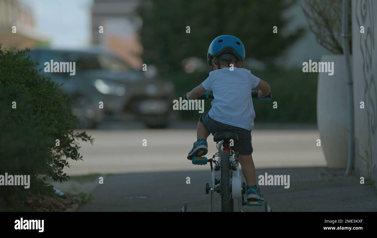 Back of child riding bicycle outside in street little boy rides bike on ...