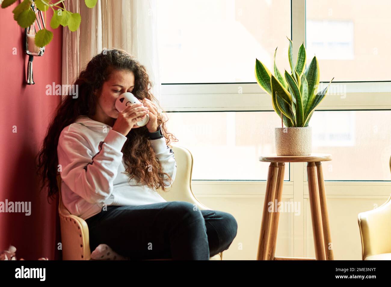 Woman relaxing in a armchair drinking a cup of tea indoors surrounded ...